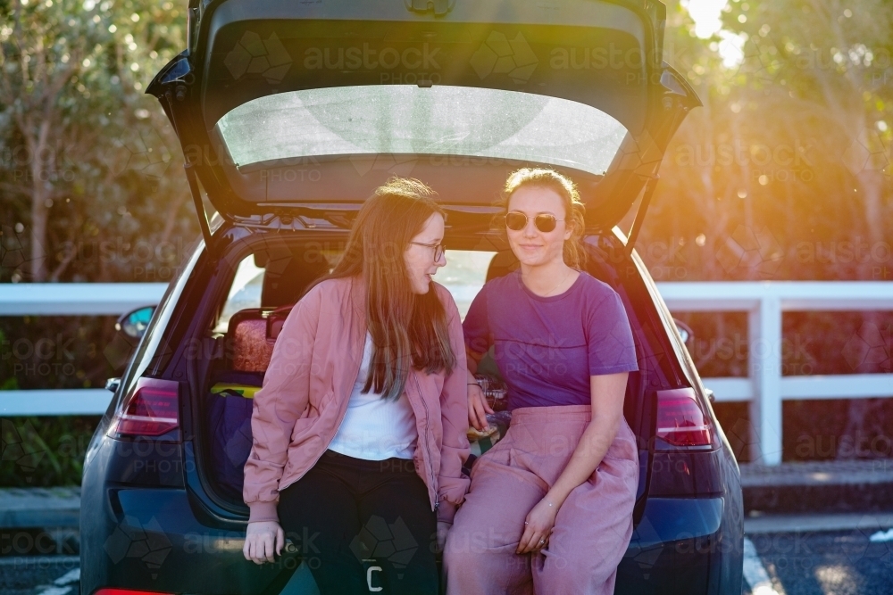 Image of 2 friends sitting on back of car - Austockphoto