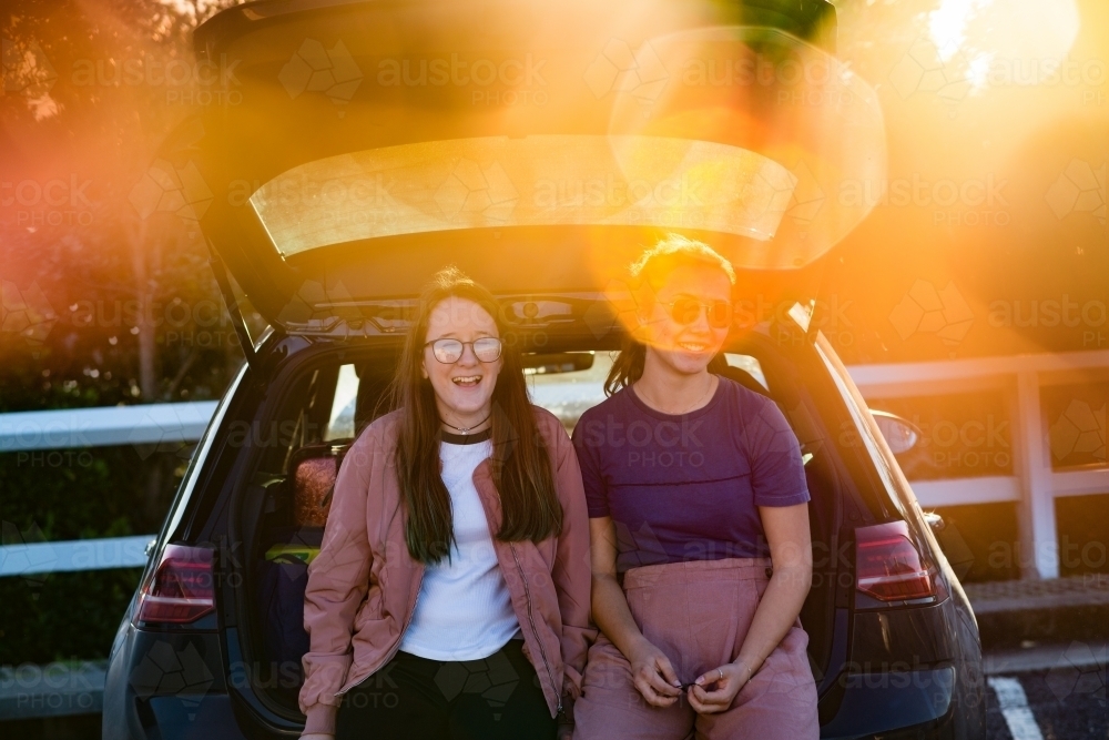 Image of 2 friends sitting on back of car - Austockphoto