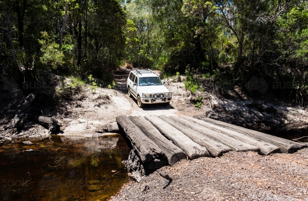 Image of 4 Wheel Drive crossing river over old tree logs - Austockphoto