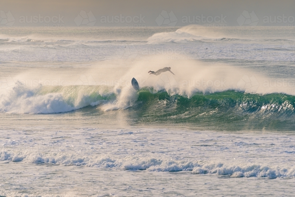 Image of A airborne surfer diving through the spray of a large crashing ...