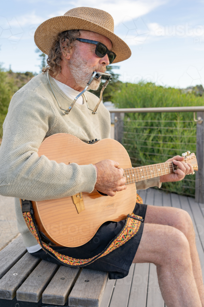 Image of A busker wearing a hat playing a guitar and harmonica on a ...