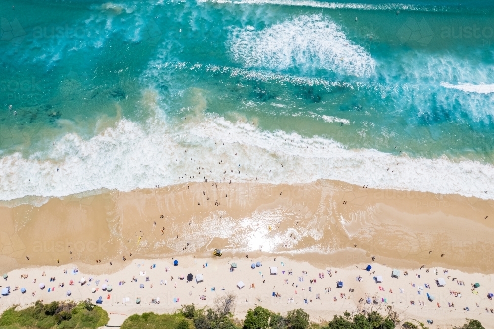 Image of A busy beach day looking down at beach goers as the surf comes ...