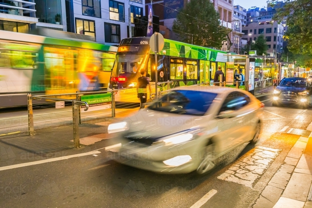Image of A car speeding past a tram in a city street at night ...