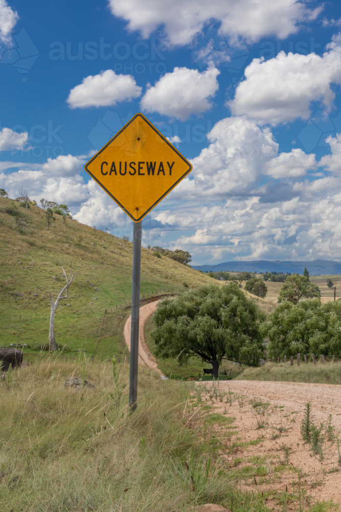 Image of A cloudy sky, a causeway sign and a country road - Austockphoto