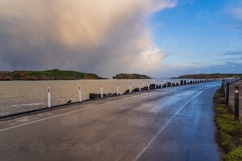 Image of A dark storm cloud advancing over a causeway road next to a ...
