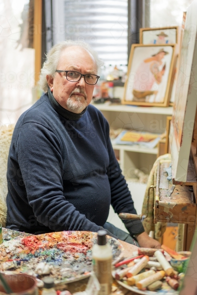 Image of A distinguished male artist sitting in front of a painting ...