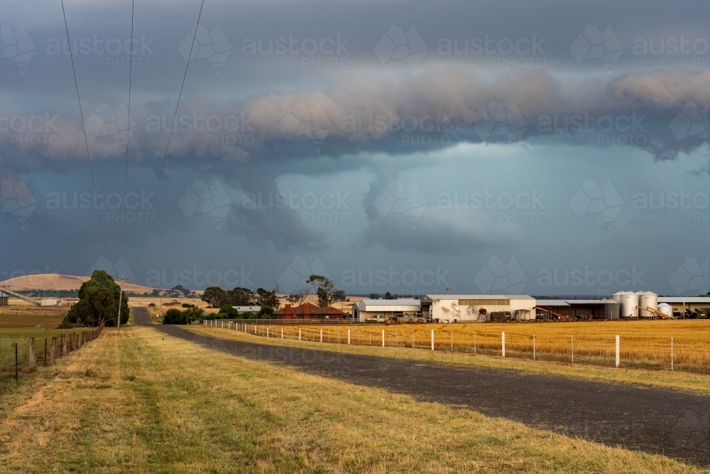 Image of A dramatic stormfront building over sheds on rural farmland ...