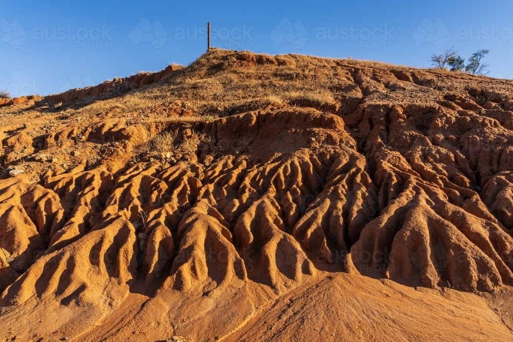 Image of A dry river bed with high eroded sides of red dirt - Austockphoto