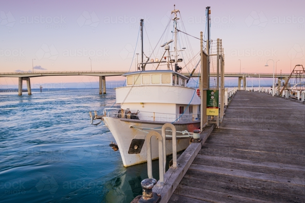 Image of A fishing boat docked at a jetty at twilight - Austockphoto