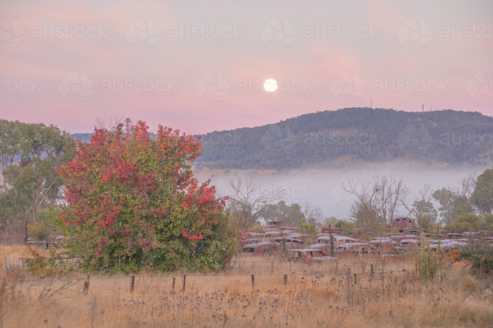 Image of A full moon in a dawn sky overlooking a misty country scene ...