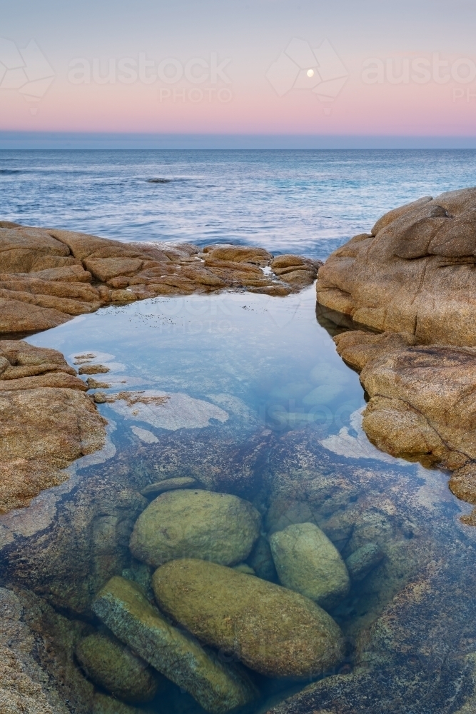 Image of A full moon rising over the ocean above a large still rock ...