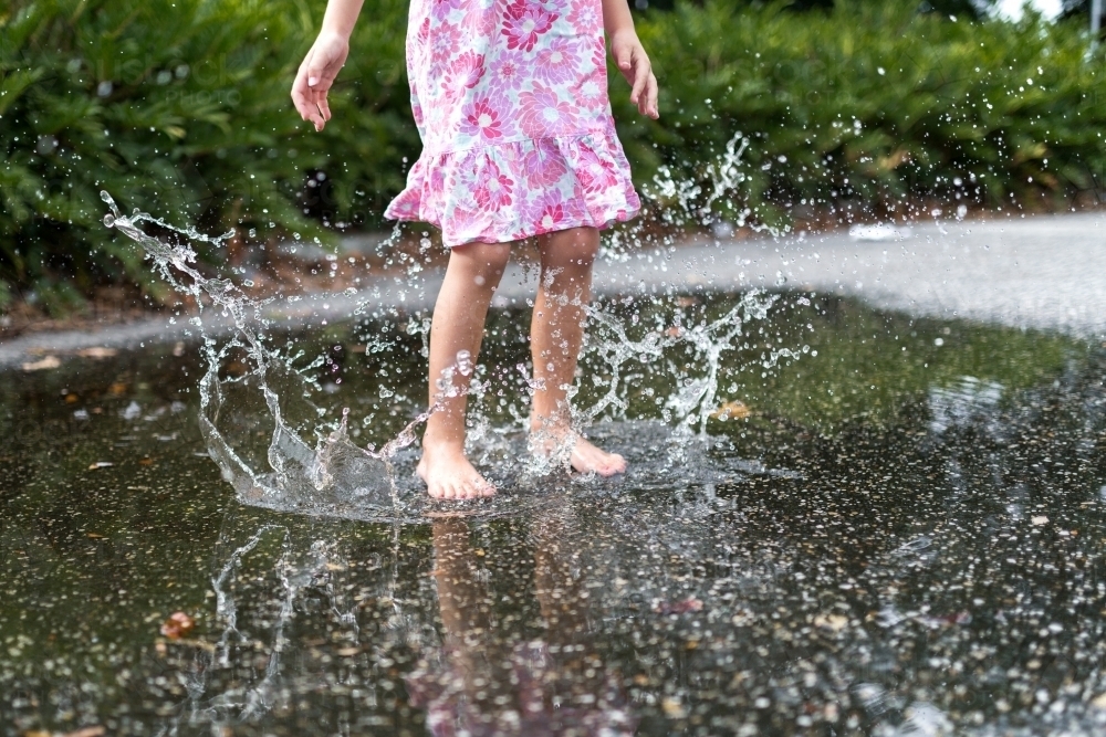 Image of A girl jumping in a puddle of water - Austockphoto