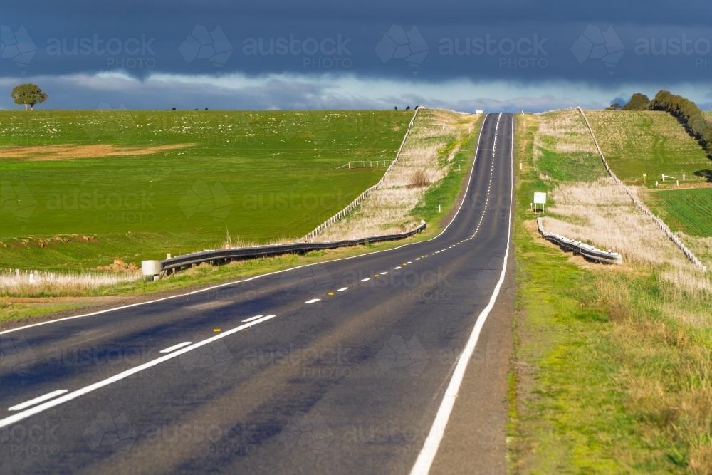 Image of A highway leading up and over a green hill on a sunny day ...