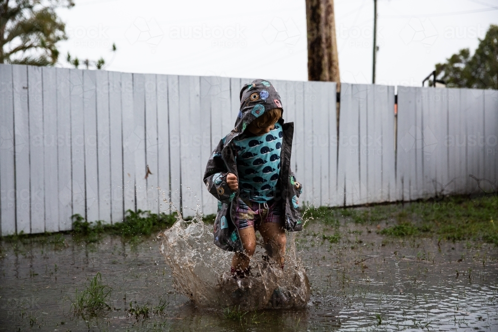Image of a kid jumping in puddles in the rain - Austockphoto