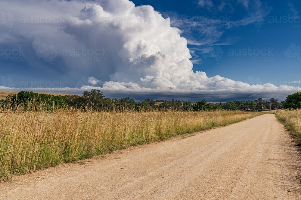 Image of A large dramatic storm cloud building over a rural dirt road ...