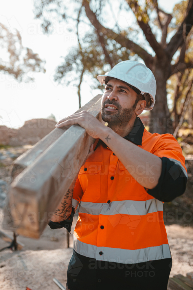 Image of A man carrying a piece of lumber on his shoulder at a ...