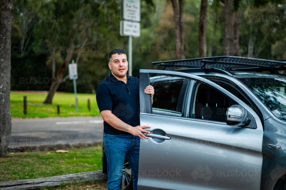 Image of A man in his thirties stands by his parked car, taking a break ...