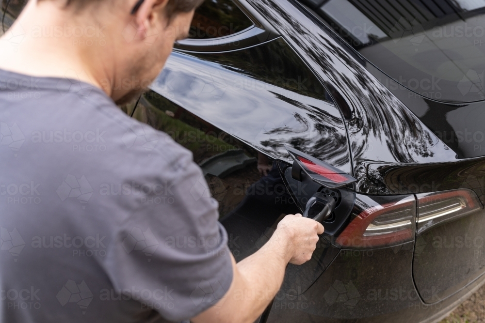Image of A man plugging in an electric Ev vehicle car to a home charger ...