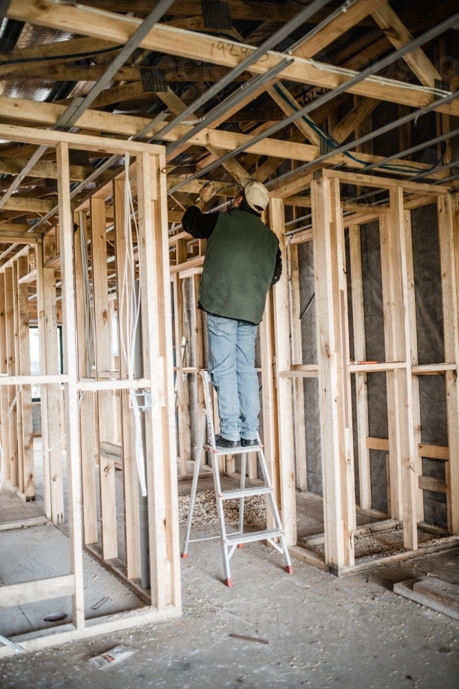 Image of A man standing on a ladder doing some cabling work inside a ...