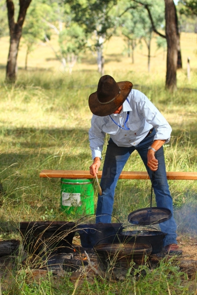 Image of A mature country lady cooking a meal in camp ovens on a fire ...