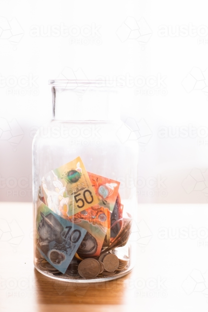 Image of a mix of australian notes and coins in a jar - Austockphoto