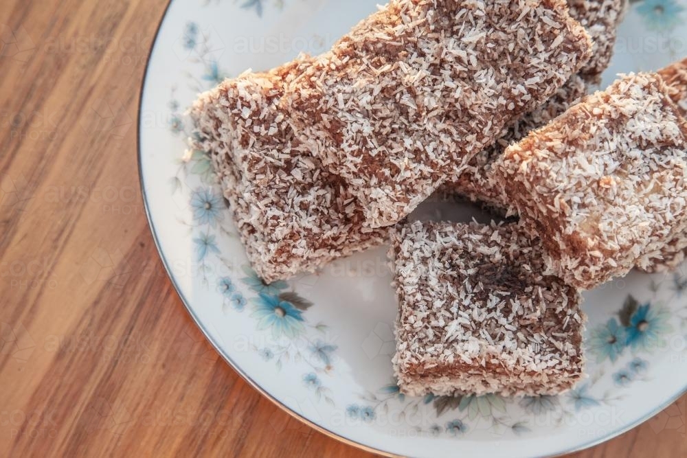 Image of A pile of lamingtons on a plate on wood table - Austockphoto