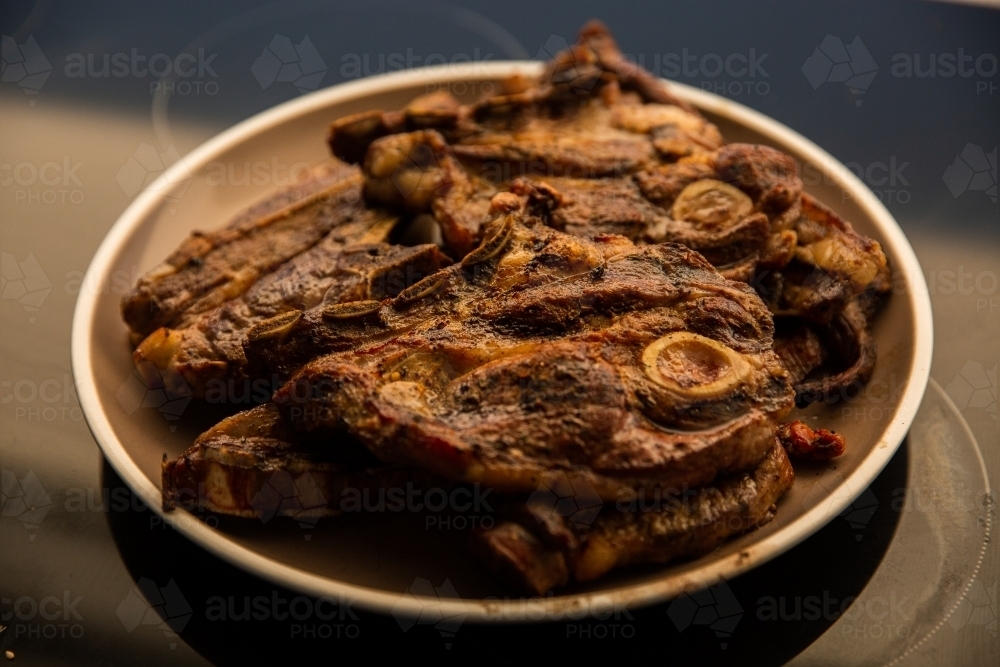 Image of a plate full of cooked lamb chops on a dark background ...