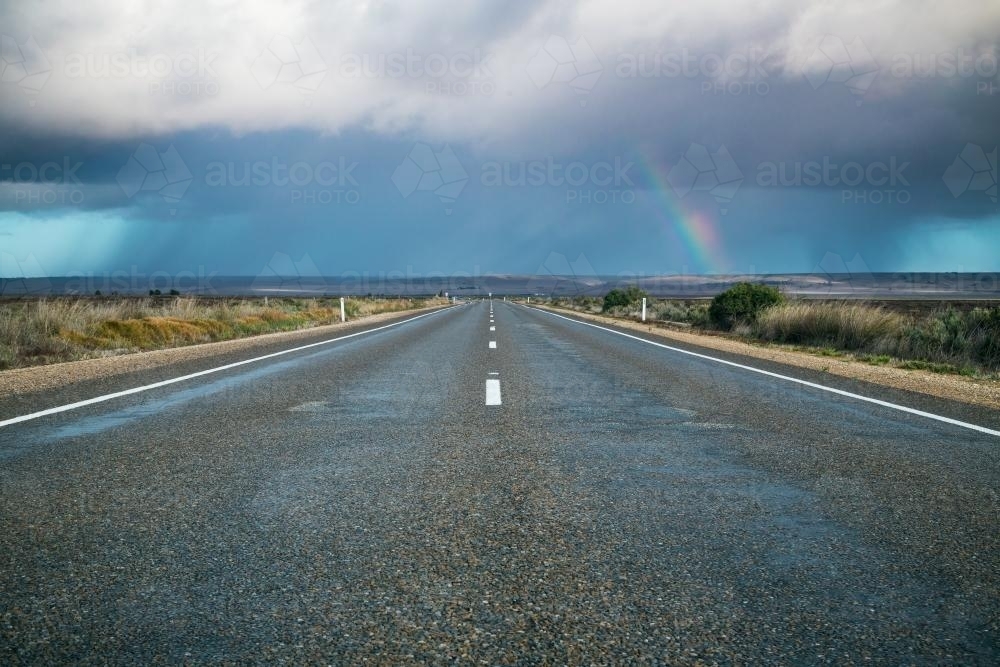 Image of A rainbow and rain falling from a cloud over a road - Austockphoto