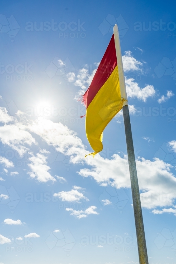 Image of A red and yellow lifesaver's flag in front of a sunny blue sky ...