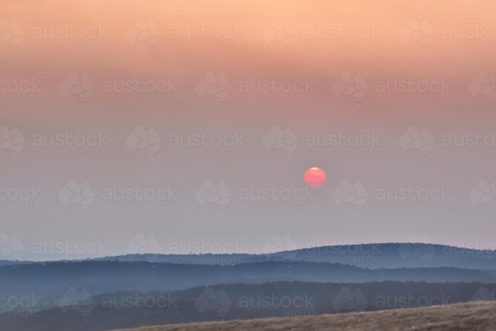 Image of A red Sun sinking into smoke haze over distant mountains ...