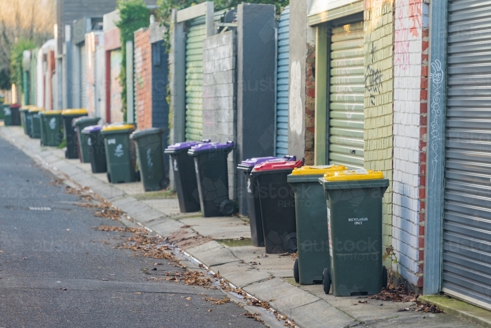 Image of A row of rubbish bins with coloured tops down an urban laneway ...