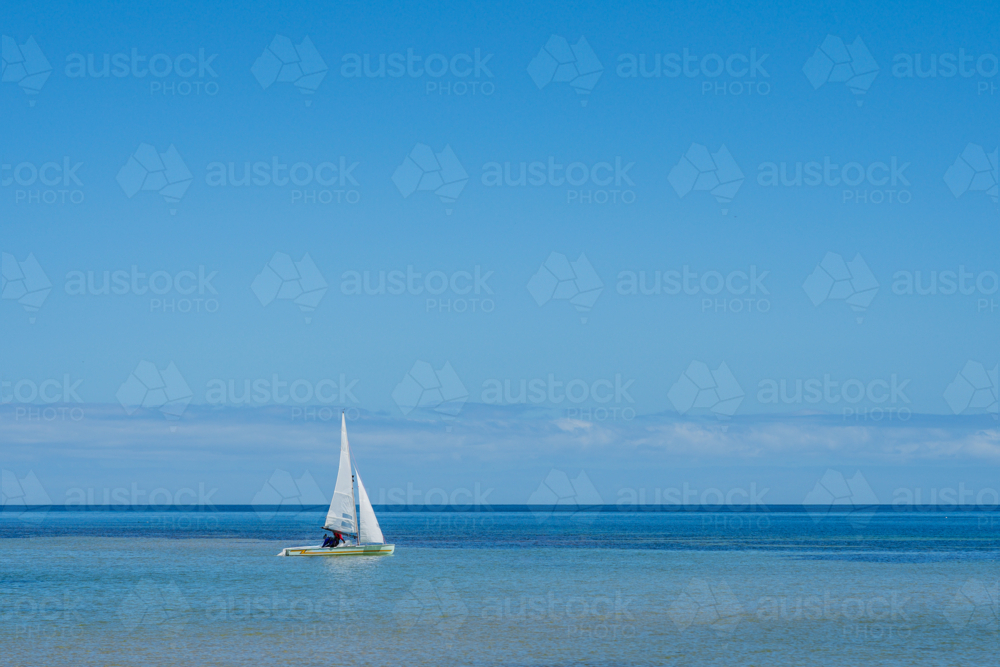 Image of A single small yacht on a coastal bay under a clear blue sky ...