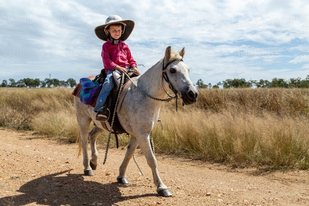 Image of A six year old boy riding his white pony on a dirt road ...