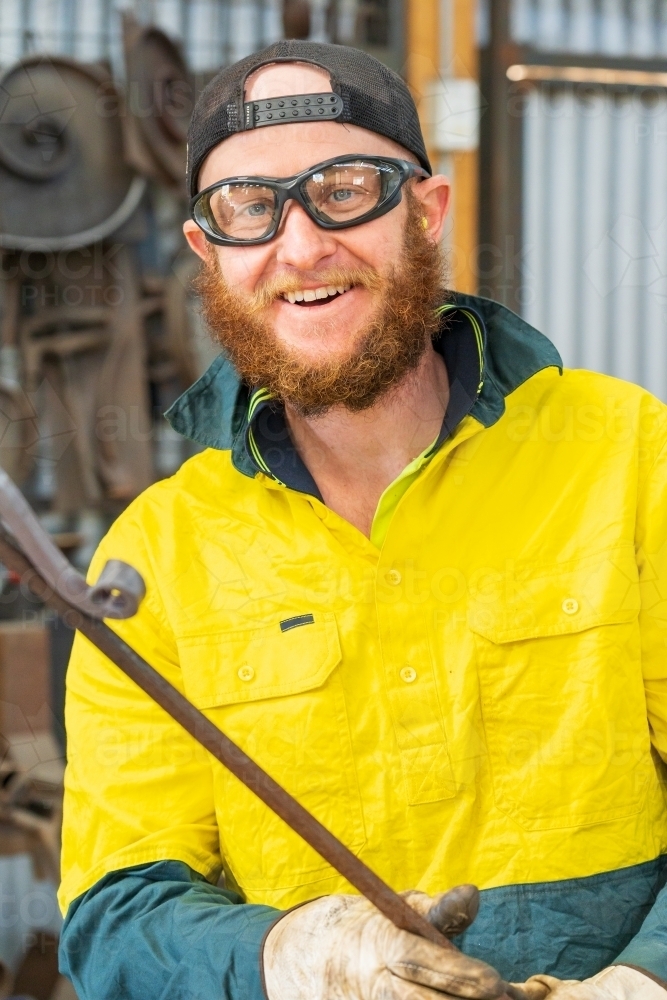 Image of A smiling bearded tradesman holding a metal rod in a workshop ...
