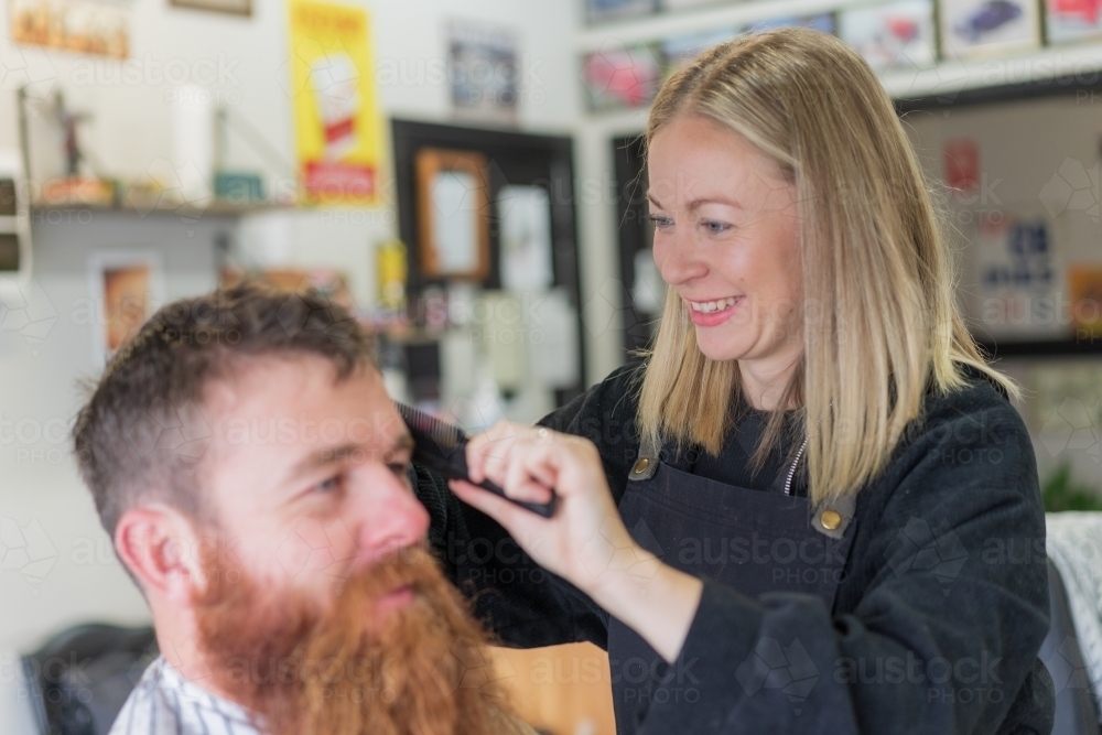 Image of A smiling woman barber giving a haircut to a man with a long ...