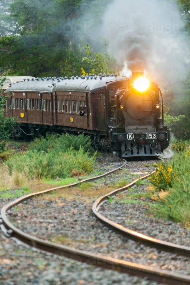 Image of A steam train tows carriages along winding railway tracks ...