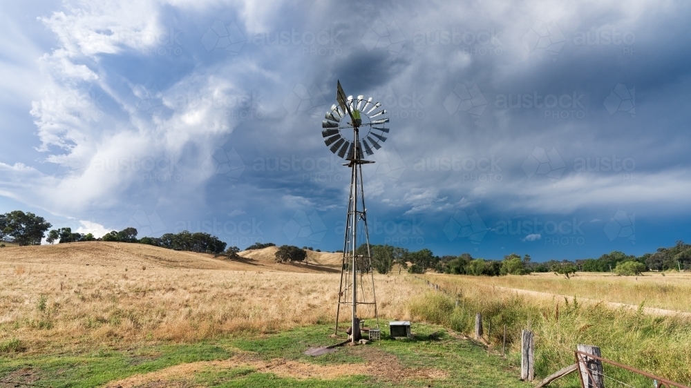 Image of A still windmill under a dramatic dark stormy sky over dry ...