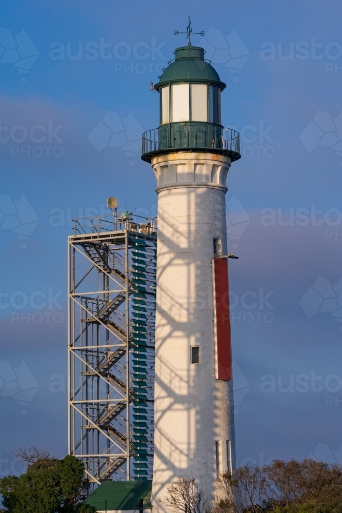 Image of A tall white lighthouse covered in shadows from a nearby light ...