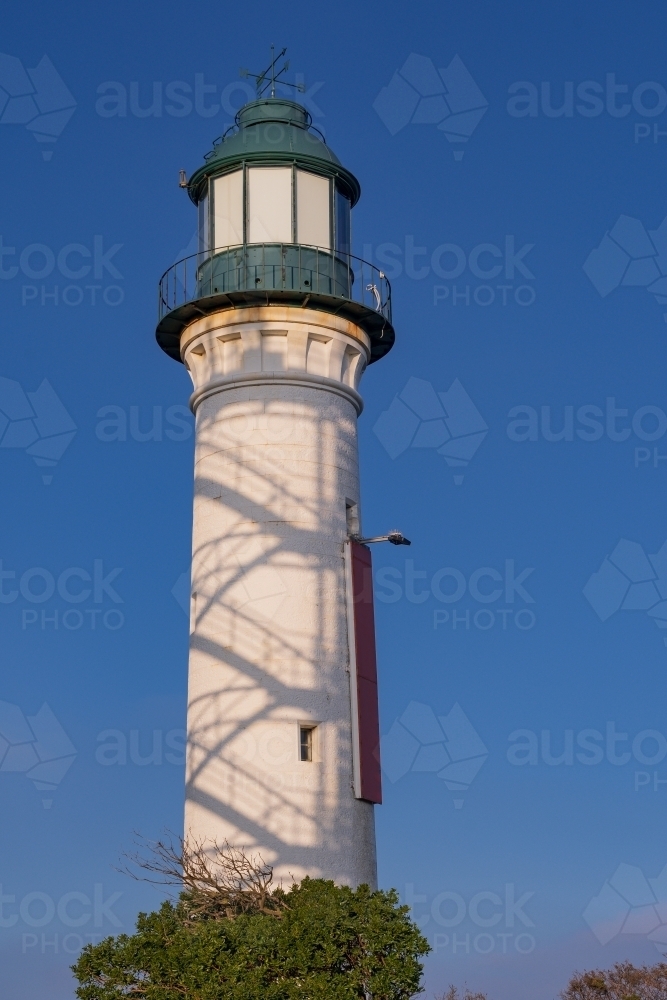 Image of A tall white lighthouse covered in shadows from a staircase ...