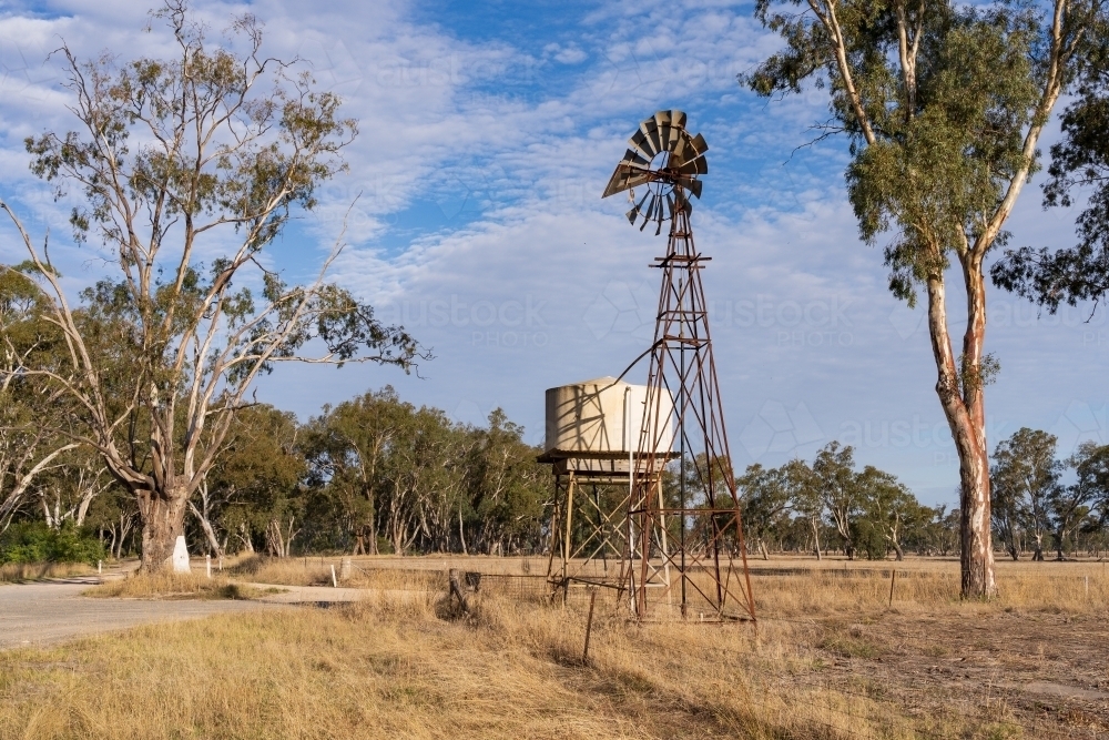 Image of A tall windmill standing next to a water tank in a rural bush ...