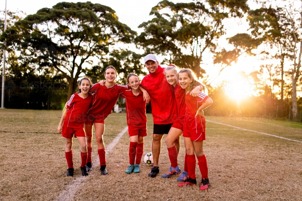 Image of A tween girls football team members standing with their coach ...