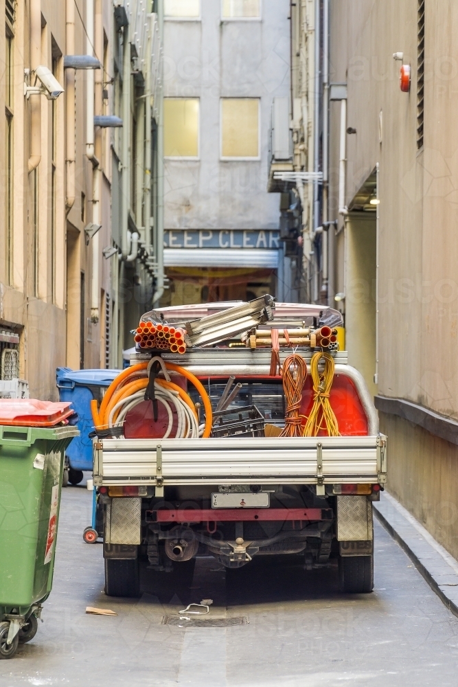 Image of A ute parked in an alley full of building equipment - Austockphoto