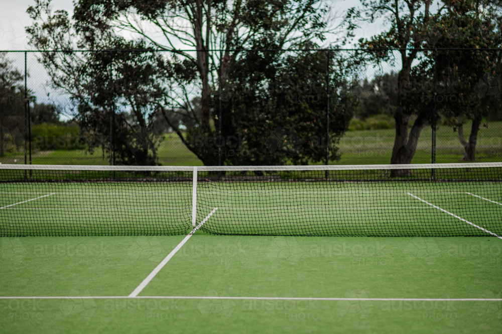 Image of A well-maintained tennis court featuring a net surrounded by ...