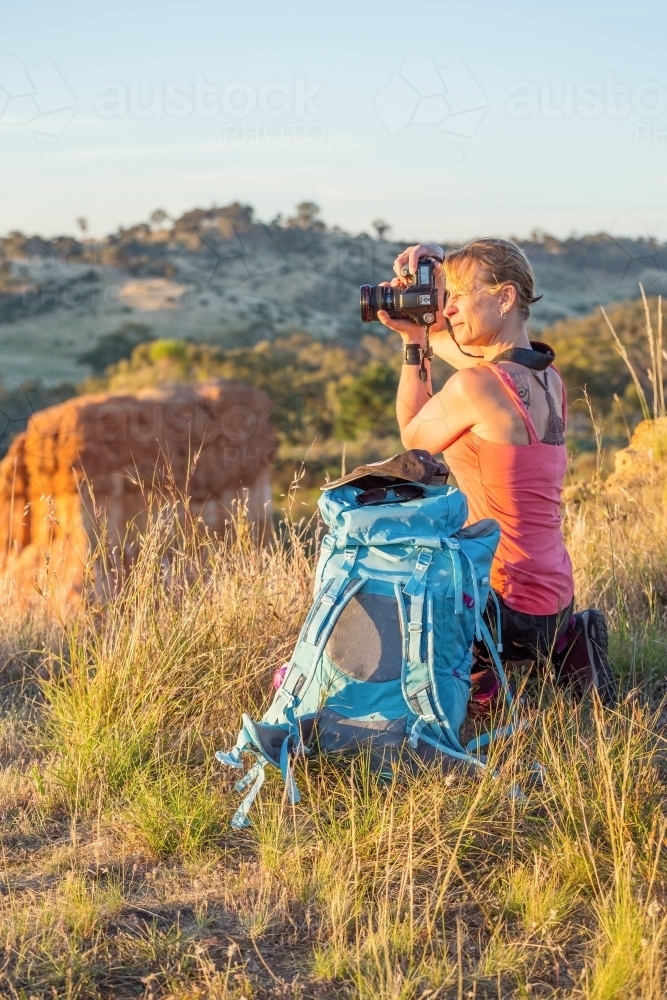 Image of A woman photographer crouching on hilltop to take a photo ...