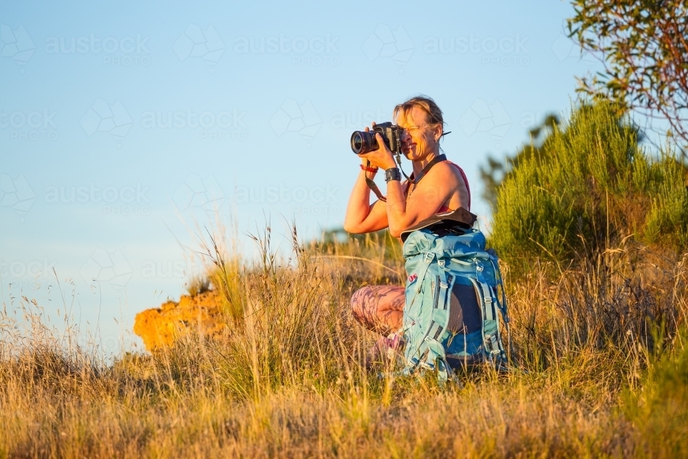 Image of A woman photographer crouching on hilltop to take a photo ...