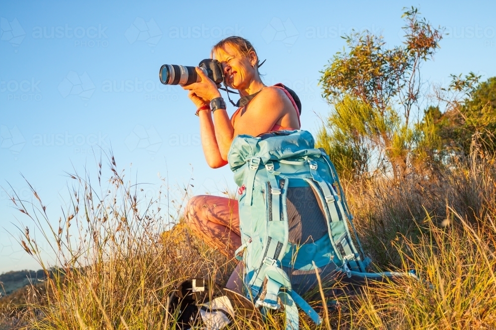 Image of A woman photographer crouching on hilltop to take a photo ...