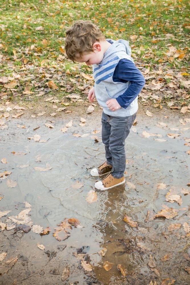 Image of A young boy jumping in a puddle of water - Austockphoto