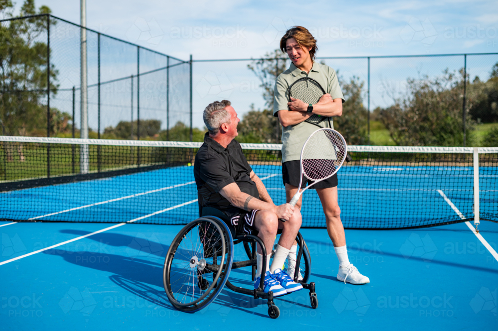 Image of A young man stands beside a seated male player in a wheelchair ...