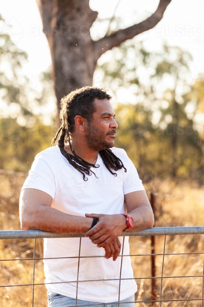 Image of Aboriginal Australian man leaning on fence looking away in ...