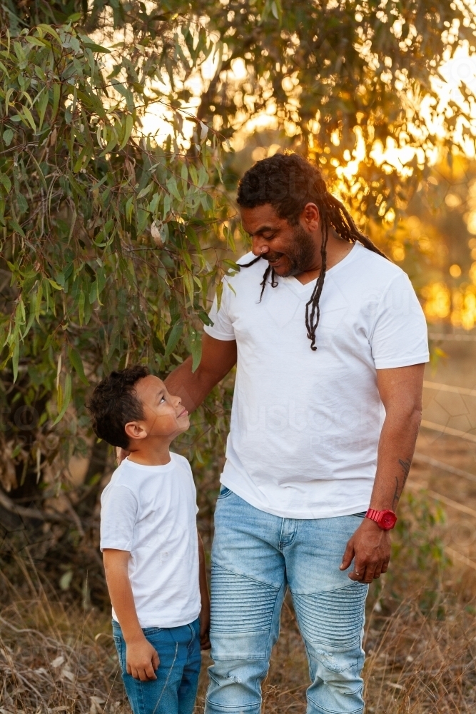 Image of Aboriginal boy looking up at dad as they stand together in ...